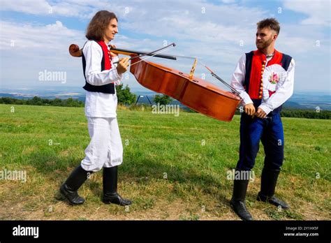 Two Men In Folk Costumes Carrying Musical Instrument And Plying On