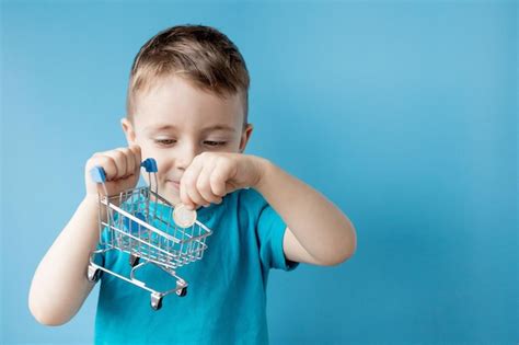 Rapaz de camiseta azul está segurando o carrinho de compras e a moeda no fundo azul conceito de