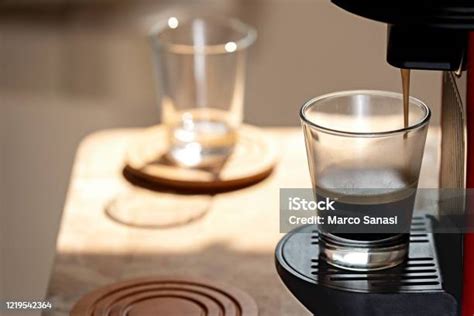두 개의 샷 안경과 전경에 샷 유리에 커피를 붓는 커피 머신의 일부와 부엌에서 나무 테이블 우정에 대한 스톡 사진 및 기타