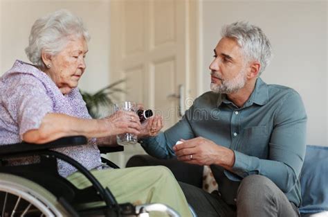 Adult Son Giving Pills To His Ill Mother Helping To Take Medication