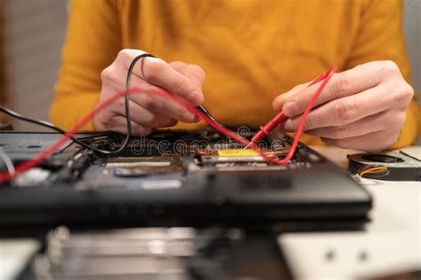 Close Up Of Man Hands Testing And Examining Laptop Motherboard With Multimeter At Desk