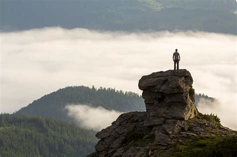 하얀 부풀어 오른 구름과 안개로 가득 산 계곡에 높은 바위 형성에 운동 등반 관광객의 실루엣과 맑은 하늘 배경 아래 상록 숲 산 슬로프로 덮여 성공에 대한 스톡 사진 및