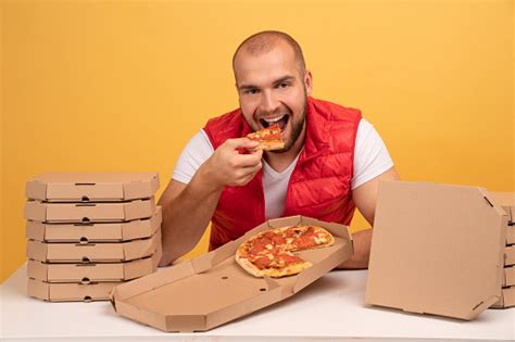 테이블에 앉아 젊은 잘 생긴 사람 피자 상자의 큰 숫자 주위에 노란색 배경 위에 피자를 먹고 가리키기에 대한 스톡 사진 및 기타 이미지 Istock