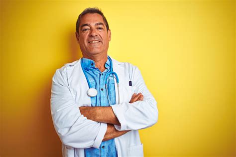 고립 된 노란색 배경 행복 한 얼굴 카메라를 보고 교차 된 팔 미소 에 청진기를 입고 잘 생긴 중년 의사 남자 긍정적 인 사람 건강관리와 의술에 대한 스톡 사진 및 기타
