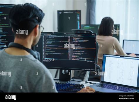 Asian Software Developers Working On Multiple Screens Displaying Code And Application Diagrams