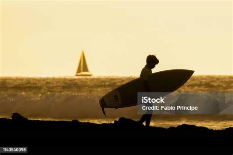 서퍼 젊은 남자는 파도와 함께 일몰 해변 바다에서 바다 해안 풍경에 자신의 손에 서핑 서 서 아름 다운 온화한 오렌지 빛 웨이크 보드 서핑의 바다 해변 실루엣에 산책 남자에