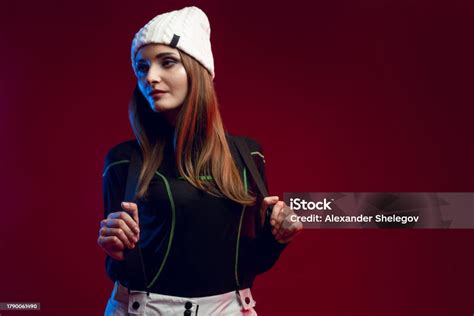 겨울 복장 재킷 스웨터 모자에 젊은 여자의 스튜디오 여성 초상화 빨간색 배경입니다 스포츠 장비 사진 소녀는 스키와 스노보드를 위해 따뜻한 옷을 입는 스포츠맨입니다 스키타기에