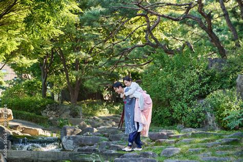 한복을 입고 숲길 또는 공원의 나무다리를 위에서 남자가 여자를 등에 업고 있는 아름답고 멋진 젊은 아시아 한국 남녀 모델