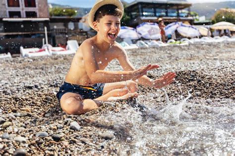 The Boy Is Having Fun On The Beach Splashing Himself With Water Stock