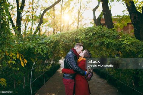 젊은 사랑 스러운 커플 아름 다운 여자와 남자 캐주얼 따뜻한 옷을 포용 하 고가 도시 공원 야외에서 녹색 아치 근처에서 키스 포옹에 사랑 관계 가족 라이프 스타일 개념입니다