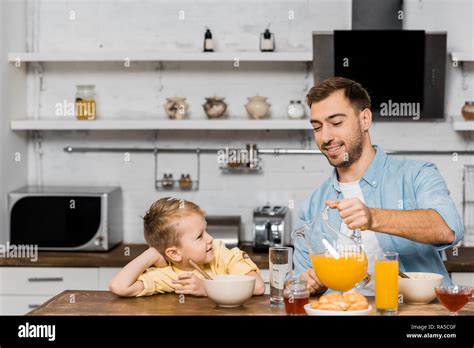 cute boy looking at smiling father pouring orange juice in glass on ...