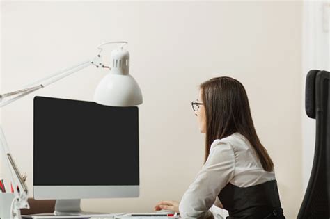 양복과 안경 보기 빛 사무실 다시 현대 모니터 컴퓨터에서 작업 하는 책상에 앉아 꽤 심각한 브라운 헤어 비즈니스 여자 와 텍스트에 대 한 장소 광고에 대 한 공간을 복사