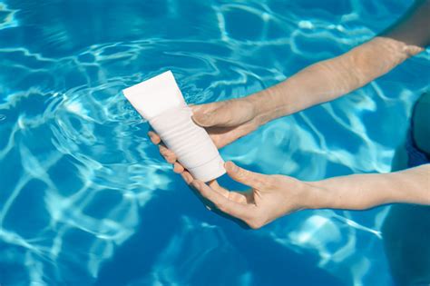 한 젊은 여성이 태양의 그림자가 있는 수영장의 푸른 물 아래에 흰색 크림 튜브를 엽니다 보습 및 자외선 차단제 피부 화장품의