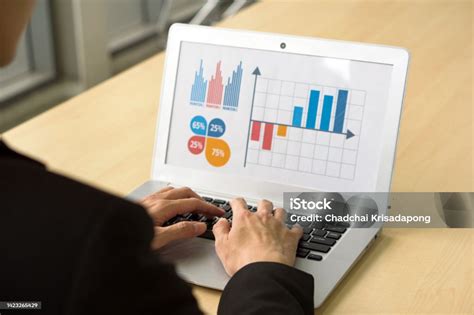 정장을 입은 사업가의 뒷모습은 사무실의 책상에 앉아 검은 색 화면이있는 랩톱 컴퓨터 키보드로 타이핑하고 그래프와 여러 가지 색상의 차트로 프리젠 테이션을합니다 개념에 대한