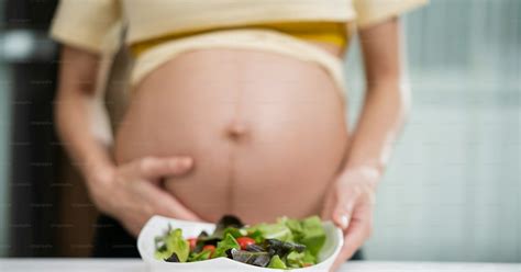 아시아 여성이 서서 야채 샐러드를 들고 있는 것을 닫습니다 매력적인 아름다운 젊은 여성 임신은 자궁에서 아기를 만지고 부엌에서 건강 식품이나 채식 음식을 선택합니다 사진