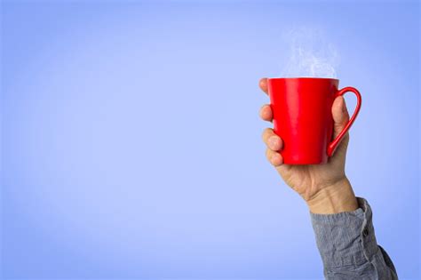 밝은 파란색 배경에 뜨거운 커피 또는 차와 빨간 컵을 들고 남성 손 따뜻한 커피 또는 차로 아침 식사 컨셉 겨울에 대한 스톡