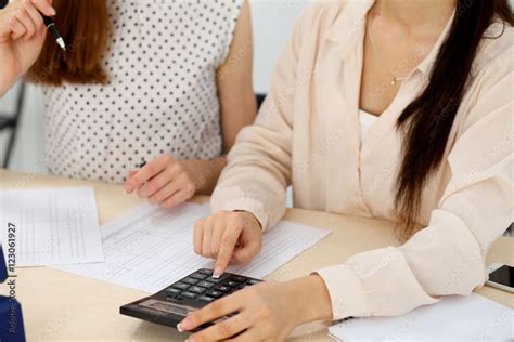 Two Female Accountants Counting On Calculator Income For Tax Form Completion Hands Closeup