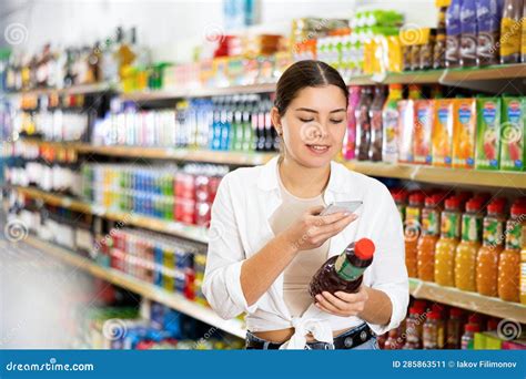 Girl Scanning Barcode On Juice Bottle With Phone In Supermarket Stock