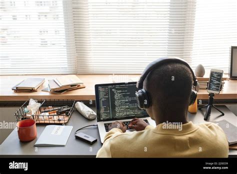 rear view of black programmer in wireless headphones sitting at desk