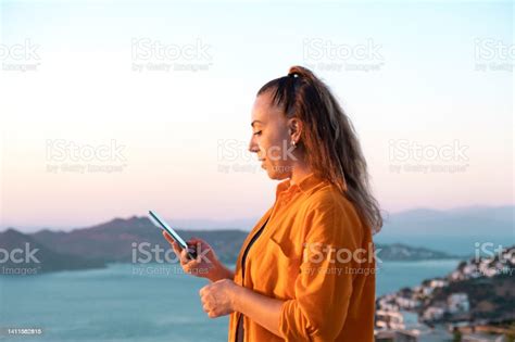 바다를 볼 수있는 테라스에서 휴대 전화를보고있는 아름다운 여성 Brand Name Smart Phone에 대한 스톡 사진 및 기타 이미지 Brand Name Smart