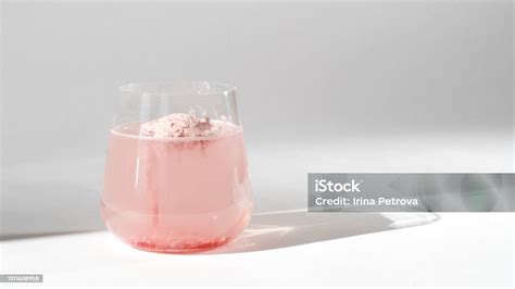 천연 딸기 콜라겐 단백질 파우더 한 잔에 물 한 잔으로 피부 재생을 위한 제품 슈퍼 푸드 트렌디 한 음식 첨가제 햇빛과 유리의 깊은 그림자와 흰색 배경 하드 햇빛 페이스