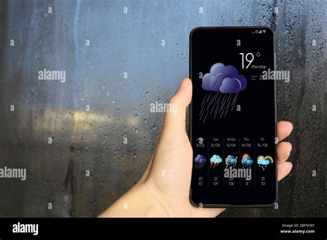 Woman Checking Weather Using App On Smartphone Near Wet Window Closeup Data Cloud With Rain