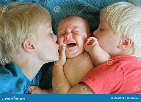 Молодые братья целуя их плача Newborn сестру младенца Стоковое Фото изображение насчитывающей