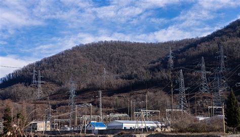 대형 전기 철탑과 송전선이 경치 좋은 풍경을 가로질러 뻗어 있으며 배경에는 산과 고요한 호수가 있어 인프라와 연결성을 상징합니다 0명에 대한 스톡 사진 및 기타 이미지