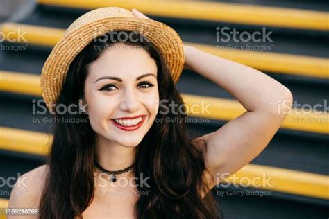 어두운 머리 건강한 피부 머리에 밀짚 모자를 쓰고 밝은 눈을 가진 쾌활한 여성은 카메라에 광범위하게 미소 머리에 그녀의 손을 유지 계단에 앉아 평온한 여성 혼자 휴식 감정