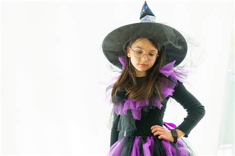 마녀 복장을 하고 안경을 쓴 귀여운 소녀가 크고 밝은 파노라마 창문 앞에 서서 포즈를 취하고 있습니다 어린이 파티와 어린 시절의 개념 10 11세에 대한 스톡 사진 및 기타