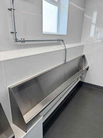Closeup Image Of Row Of Stainless Steel Urinal Troughs In Public