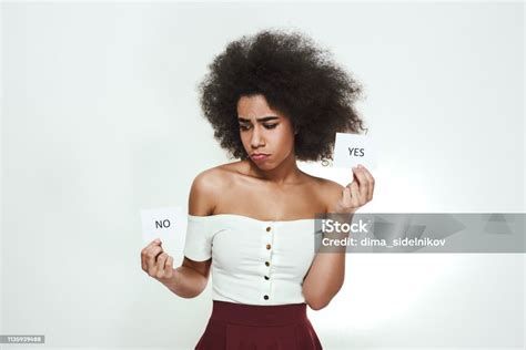 나는 확실 하지 않다 혼란 스러운 젊은 아프리카 사람 미국인 여자는 회색 배경에 서 있는 동안 그들에 게 예 및 아니오와 함께 논문을 들고 생각 가까이 옴에 대한 스톡 사진