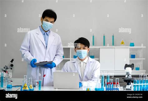 Two Scientists With Face Mask And Gown Working In Laboratory Omicron Strain Testing Process