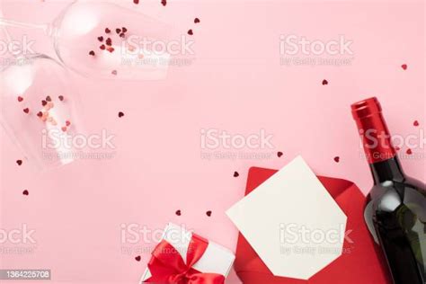 카피 스페이스와 고립 된 파스텔 핑크 배경에 카드와 와인 병과 빨간색 활 레드 봉투와 발렌타인 데이 장식 와인 안경 하트 모양의 색종이 흰색 선물 상자의 최고 보기 사진