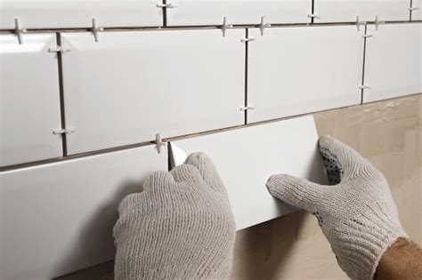 부엌 벽에 세라믹 타일을 깔고 있는 남자 노동자 마스터 수리공은 흰색 현대 타일을 배치하고 접착제를 뿌립니다 수리 리노베이션 작업에서 타일을 설치하는 빌더 전문 타일링 4