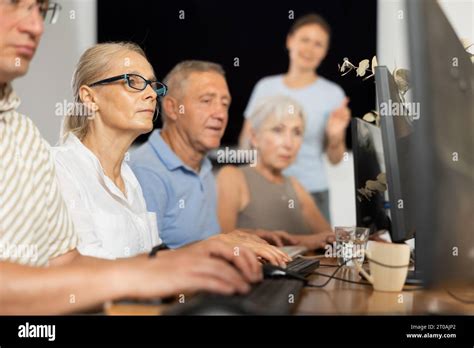 elderly woman mastering computer skills during group course with mentor