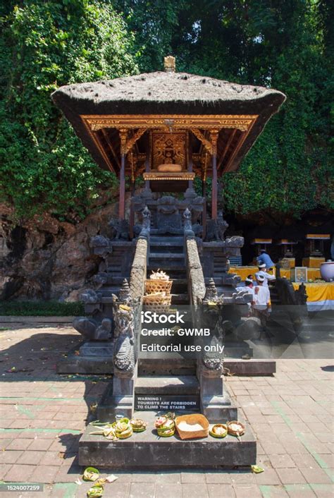 푸라 고아 라와 사원 또는 이스트 발리 고아 라와에 있는 박쥐 동굴 사원 내부의 장면으로 바위 면의 기슭에 박쥐 동굴이 보입니다 사람들은 발리 전통 의상을 입고 카낭 사리와