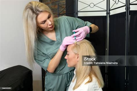 삼차 전문의 금발 여성 모발 메조 테라피 절차를 수행하는 미용사 백인 의사는 주사기로 두피 주사를합니다 생체 자극 유모 세포