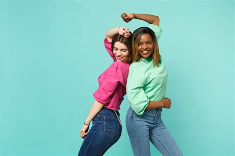 두 젊은 여자 친구 블루 청록색 벽 배경 스튜디오 초상화에 고립 된 장난 춤 분홍색 녹색 옷에 유럽과 아프리카계 미국인 사람들 라이프 스타일 개념입니다 복사 공간을 모의