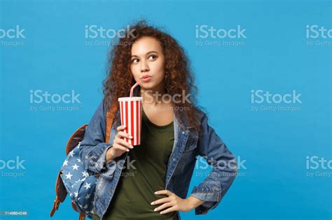 데님 옷에 젊은 아프리카계 미국인 소녀 십 대 학생 배낭 홀드 종이 컵 파란색 배경 스튜디오 초상화에 고립 고등학교 대학 대학 개념에서 교육 복사 공간을 모의 합니다 가방에