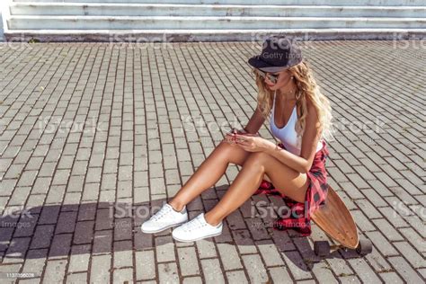 스케이트 보드와 스포츠 소녀 도시의 롱 보드 여름 그녀의 손에서 유행 여자 전화 인터넷 소셜 네트워크 채팅 안경 및 야구 모자 검게 그을린 피부와 슬림 그림 여유 공간