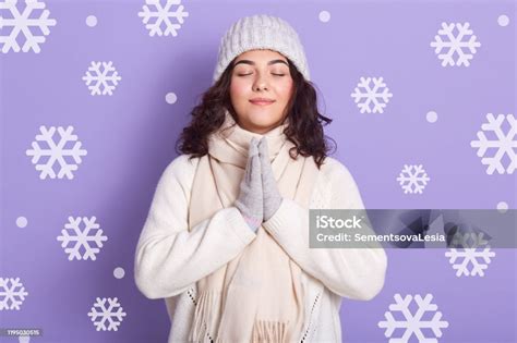 예쁜 아가씨의 초상화 모자를 입고 장갑 스웨터 서서기도 가슴 앞에서 함께 손을 유지 닫힌 눈으로 포즈 어두운 물결 모양의 머리를