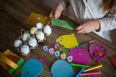 한 아이가 나무 탁자 위에서 펠트와 종이로 공예품을 만들고 있습니다 근처에는 장식용 달걀 끈적끈적한 눈 반짝이 페인트 색연필이 있습니다 창의적인 과정 부활절 및 어린이