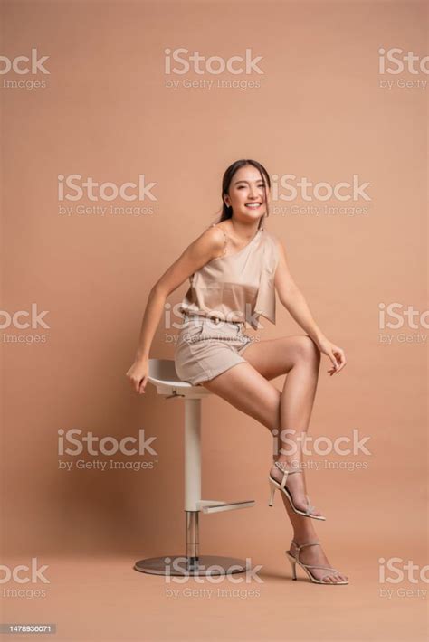 자신감 매력적인 세련된 아시아 여성 럭셔리 드레스 천 흰색 의자에 앉아 쾌활한 미소 긍정적 인 감정을 즐길 수 손 제스처 따뜻한 환영 카메라 초상화 스튜디오에서 촬영 컬러