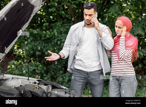 Sad Despaired Arab Woman In Hijab And Man Call To Auto Support Stand Near Broken Car With Open