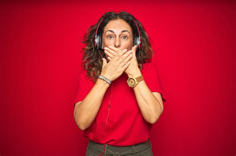 빨간 고립 된 배경을 통해 음악을 듣고 헤드폰을 착용 중년 여성은 실수로 손으로 입을 덮는 충격 비밀 개념입니다 한 명의 여자만에 대한 스톡 사진 및 기타 이미지 Istock