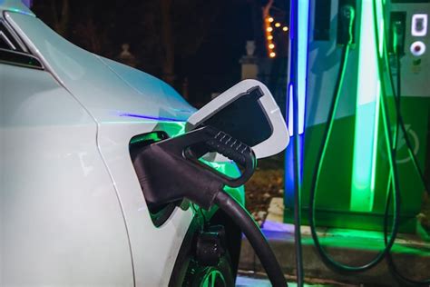 Premium Photo The White Car Is Connected To The Electric Charging Station At Night In Neon Lights