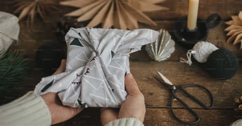 장식품이 있는 소박한 나무 테이블에 현대적인 축제 패브릭으로 포장된 크리스마스 선물을 들고 있는 손 분위기 있는 분위기 있는 이미지 북유럽 스타일 즐거운 성탄절