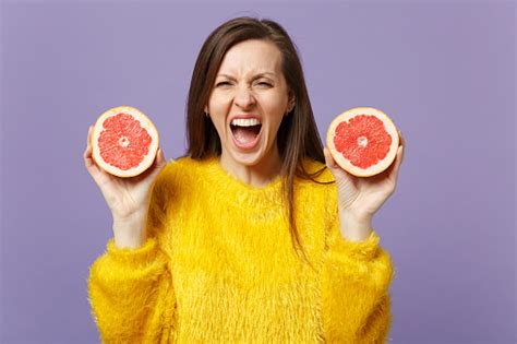 스튜디오에서 보라색 파스텔 배경에 고립 된 신선한 익은 자 몽의 Halfs를 들고 모피 스웨터에 미친 비명 젊은 여자 사람들은 생생한 라이프 스타일 휴식 휴가 개념입니다