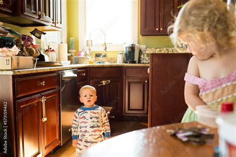 Big Sister Looks Back At Camera Aware Little Brother In Messy Kitchen